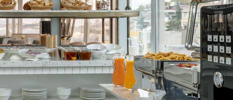 Disposição de buffet com diversos alimentos, uma máquina de café e um dispensador de suco.