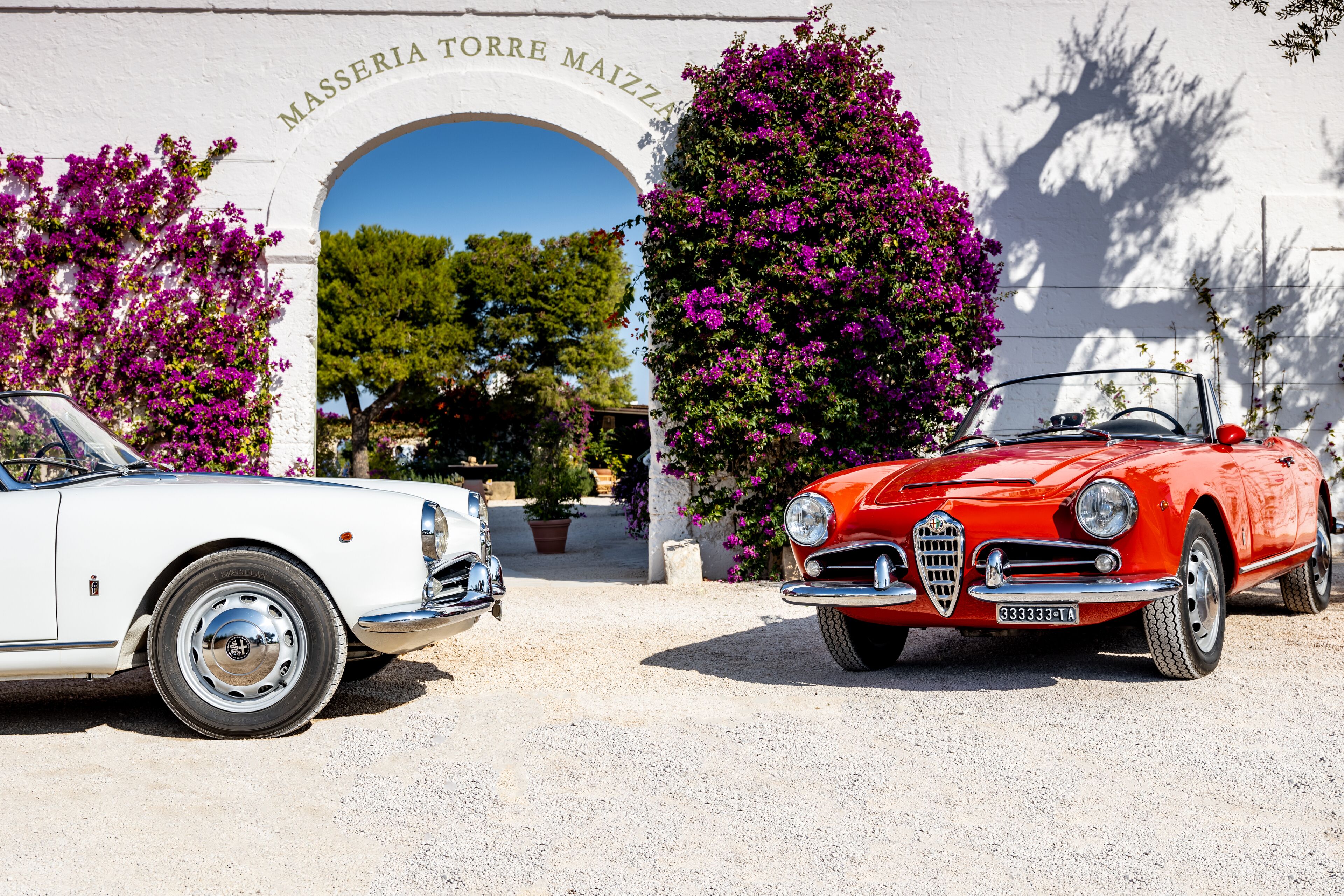 Dois carros antigos estacionados em frente a um edifício com um arco com a inscrição "MASSERIA TORRE MAIZZA".