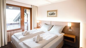 Uma cama de casal com roupa de cama e toalhas brancas, cabeceira de madeira, abajures e uma obra de arte emoldurada na parede.