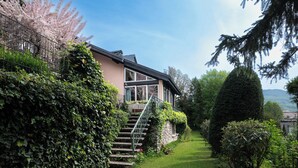 Uma casa com escadaria de pedra que leva a uma varanda, cercada por vegetação exuberante e um céu claro.