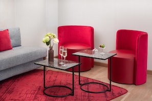 Uma sala de estar moderna com um sofá cinza, cadeiras vermelhas, uma mesa pequena com dois copos e um vaso com flores.