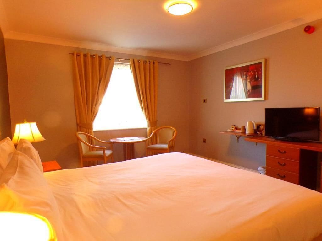 Quarto de hotel com cama, escrivaninha, cadeira, televisão e janela com cortinas.