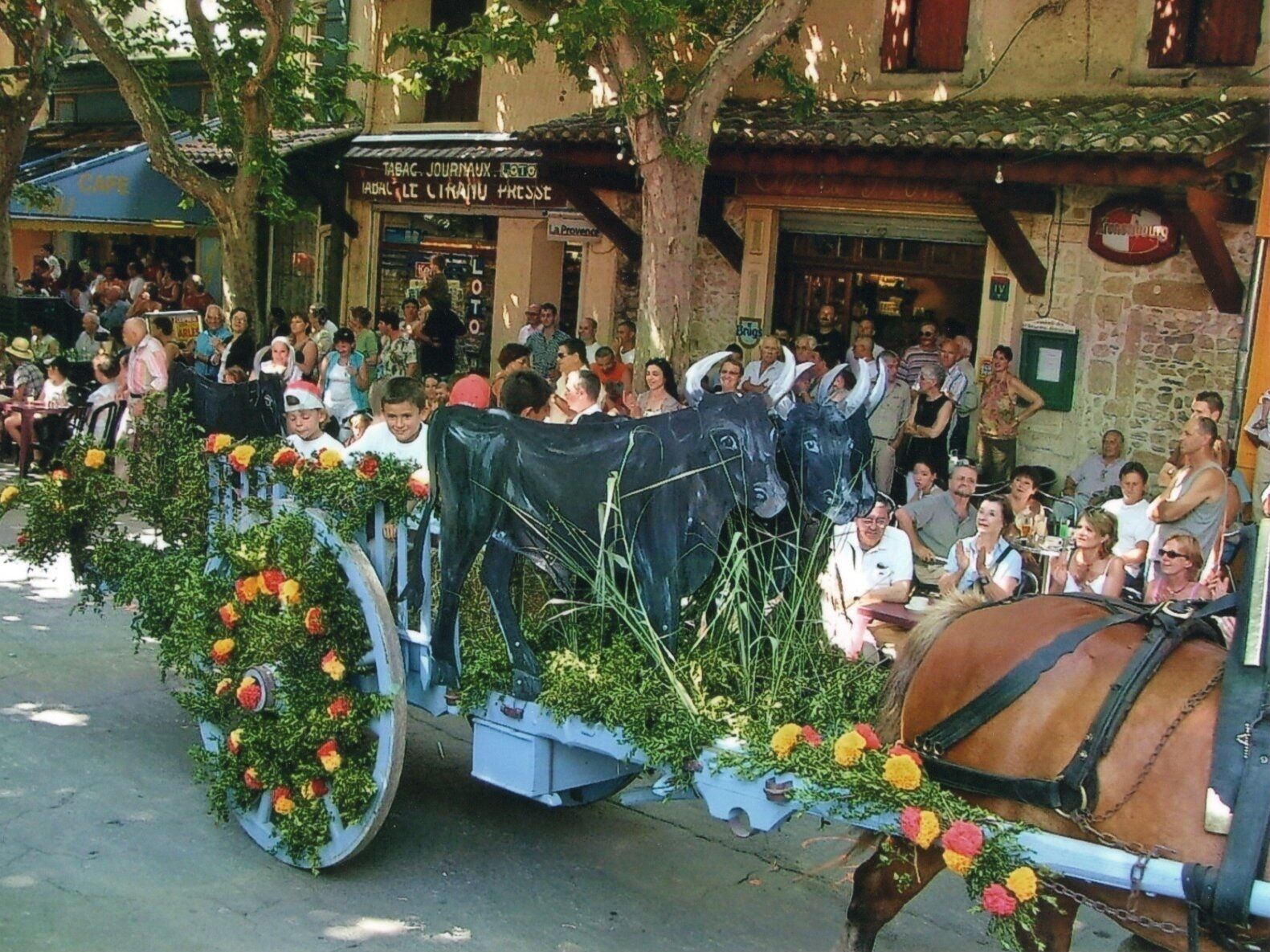 Um carro alegórico de parade com um cavalo e dois touros negros grandes, cercado por espectadores.