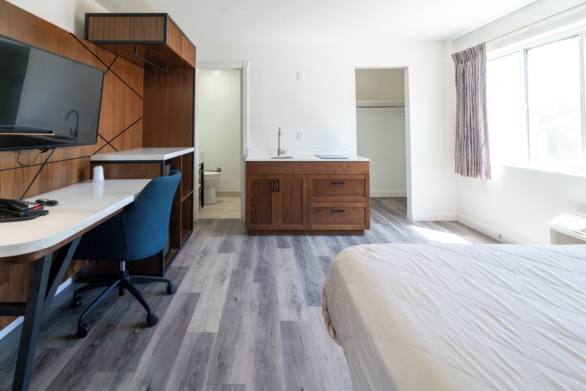 Quarto com cama, escrivaninha, cadeira, televisão e banheiro.