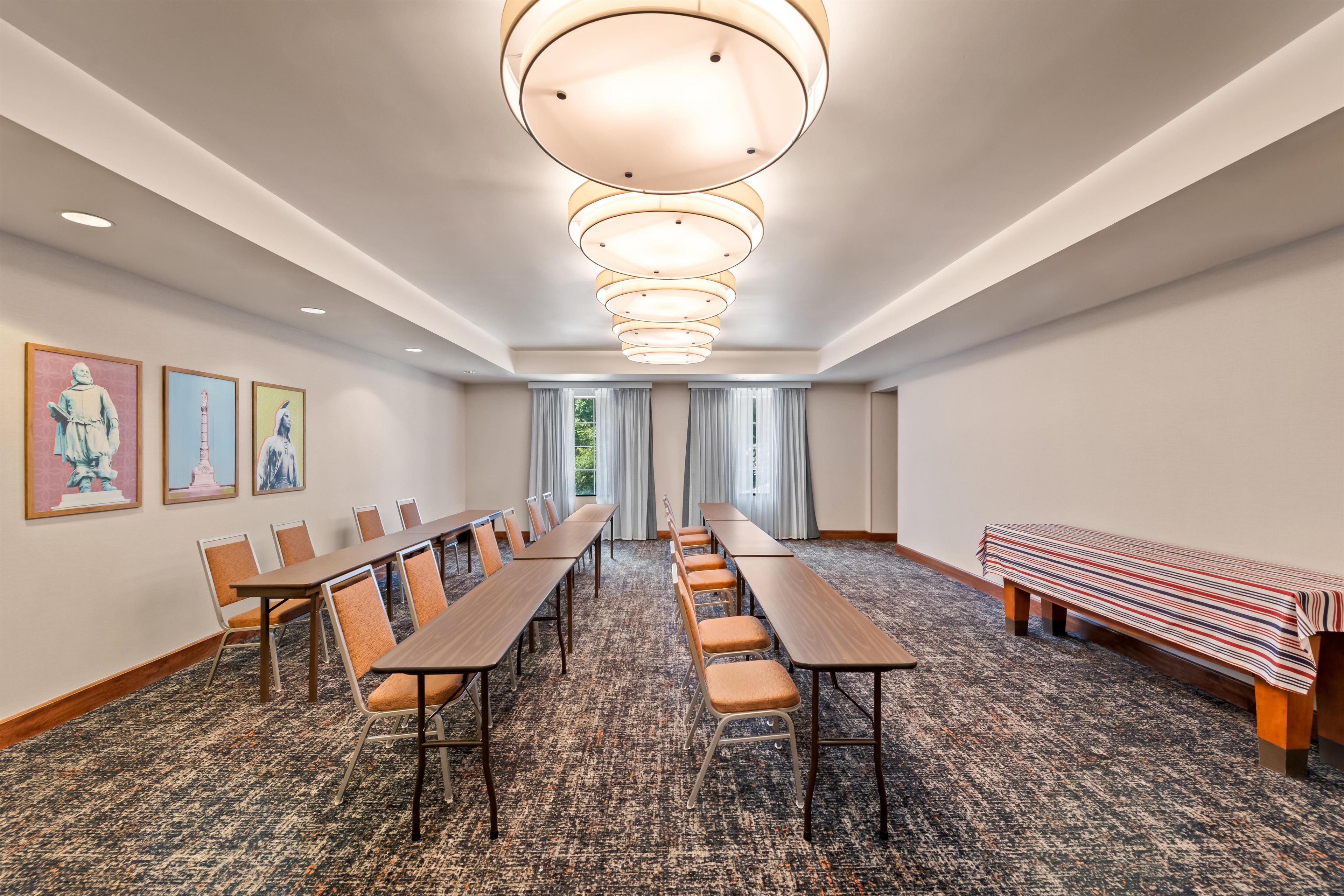 Uma sala de conferências com mesas compridas, cadeiras e um banco.