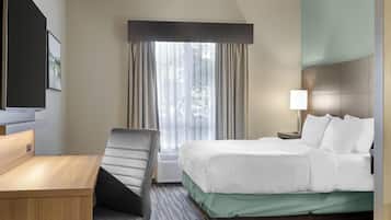 Quarto de hotel com cama, escrivaninha, cadeira, mesa de cabeceira e janela com cortinas.