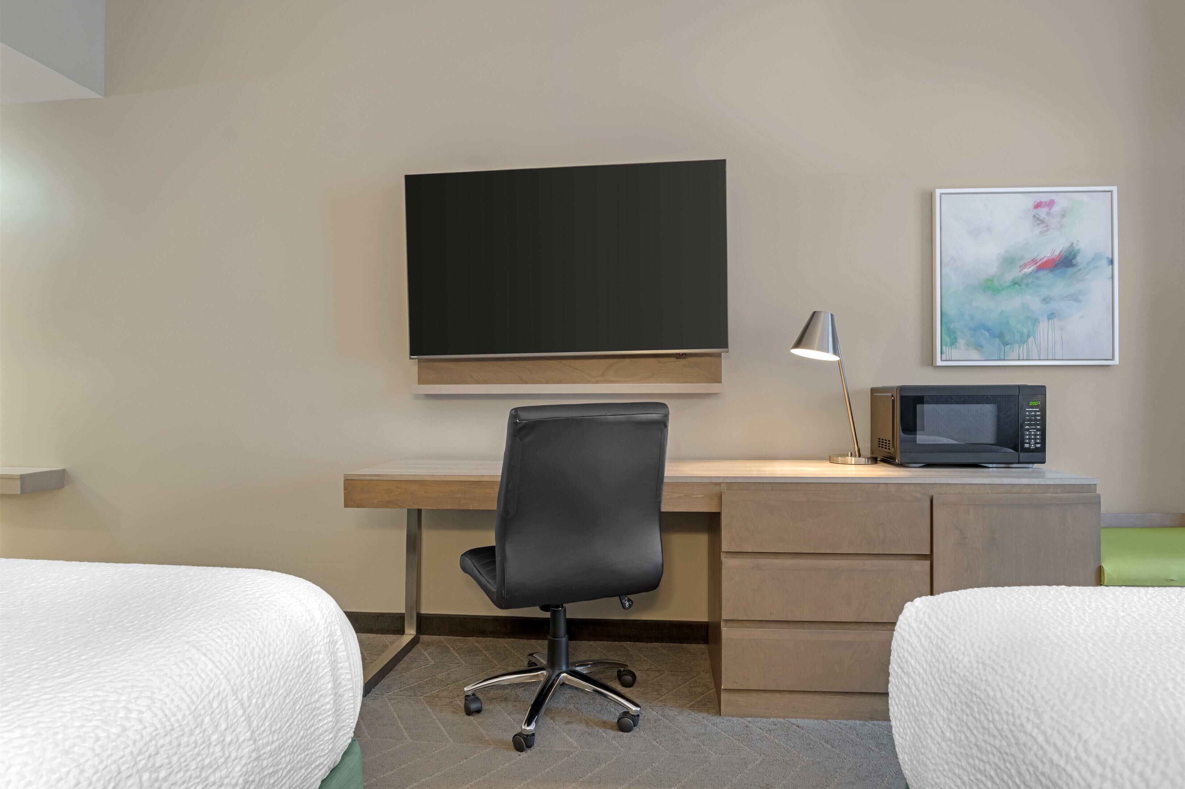 Quarto de hotel com uma cama, uma mesa de escritório com um computador, uma televisão e um micro-ondas.