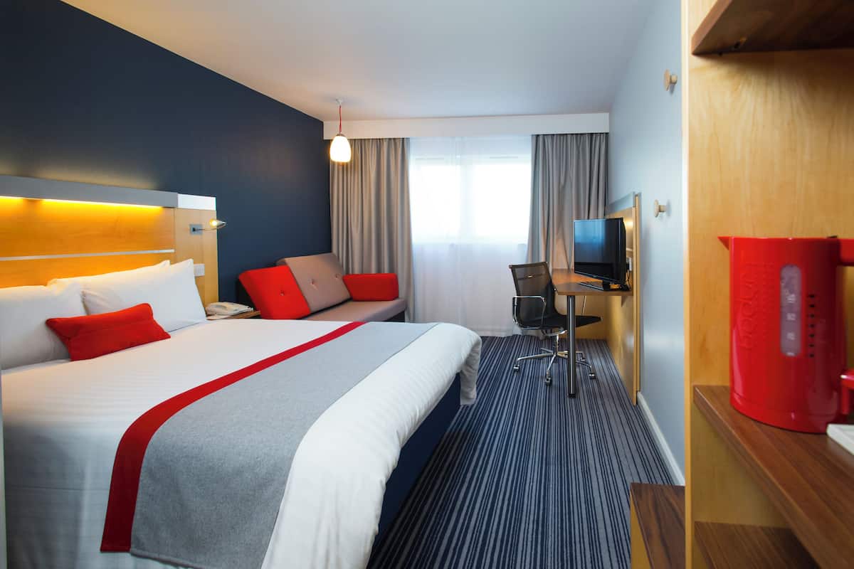 Quarto de hotel com uma cama grande, uma escrivaninha, uma cadeira, uma televisão e uma máquina de café vermelha.