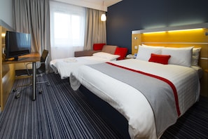 Quarto de hotel com duas camas, uma mesa de escritório e uma televisão.