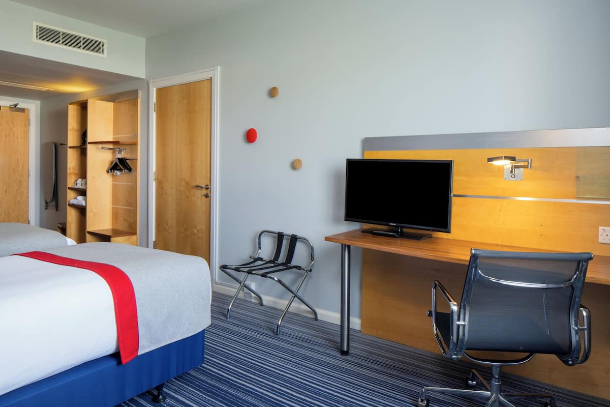 Quarto de hotel com uma cama, uma secretária com televisão, uma cadeira e um guarda-roupa.