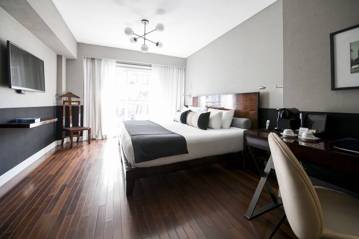 Quarto de hotel com uma cama grande, uma escrivaninha com cadeira, televisão e vista para o exterior.
