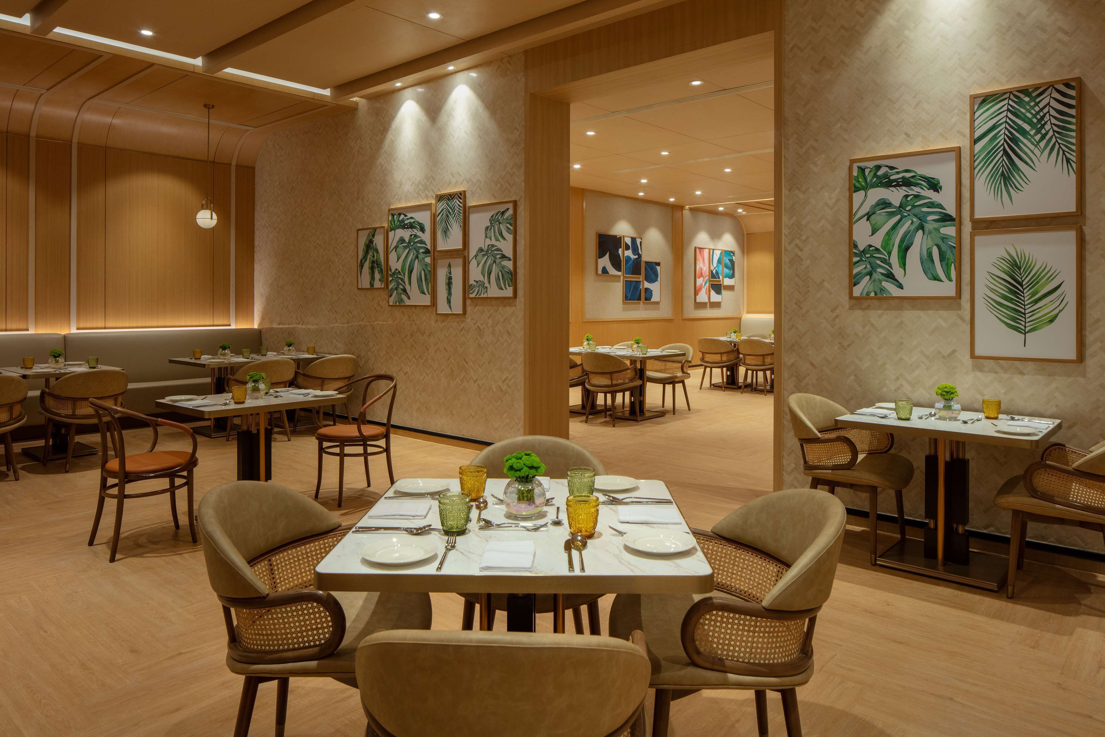 Um restaurante com várias mesas e cadeiras, apresentando um interior moderno com painéis de madeira e obras de arte nas paredes.