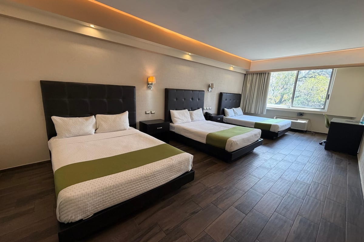 Quarto de hotel com duas camas, uma escrivaninha, uma cadeira e uma janela com cortinas.