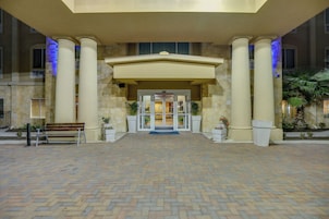 Entrada de hotel com calçada de tijolos, um banco e porta dupla.