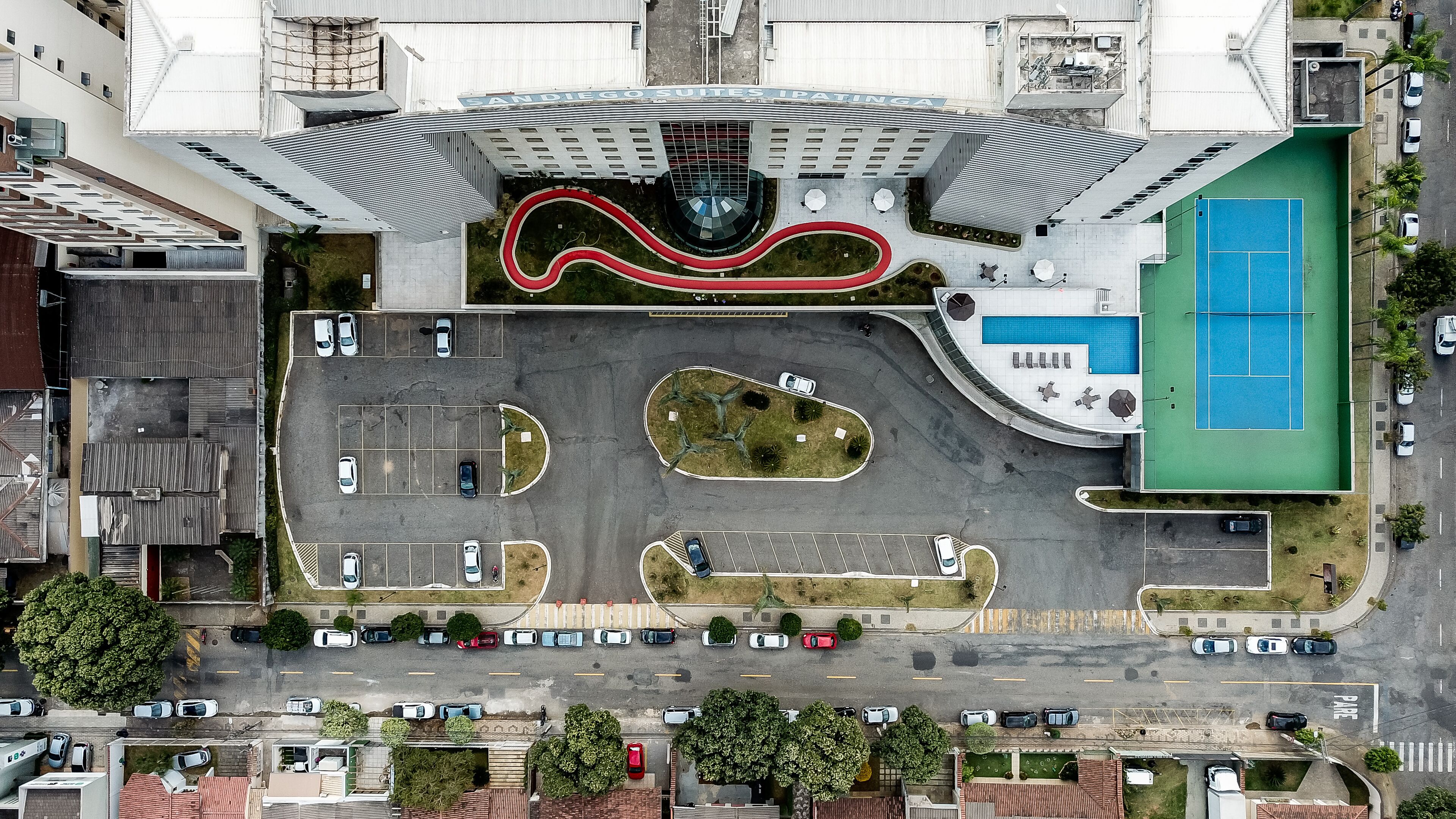 Vista aérea de um complexo hoteleiro com vários edifícios, estacionamento e quadra de tênis.