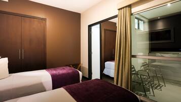Quarto de hotel com duas camas, um guarda-roupa, um painel de vidro e um pequeno espaço para sentar.