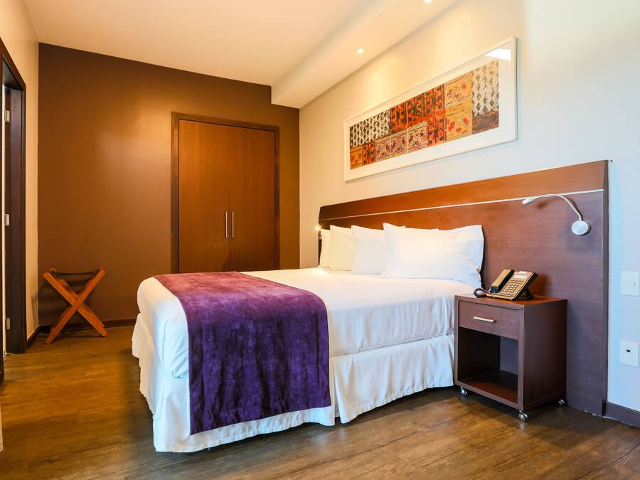 Quarto de hotel com cama, mesa de cabeceira e um quadro na parede.