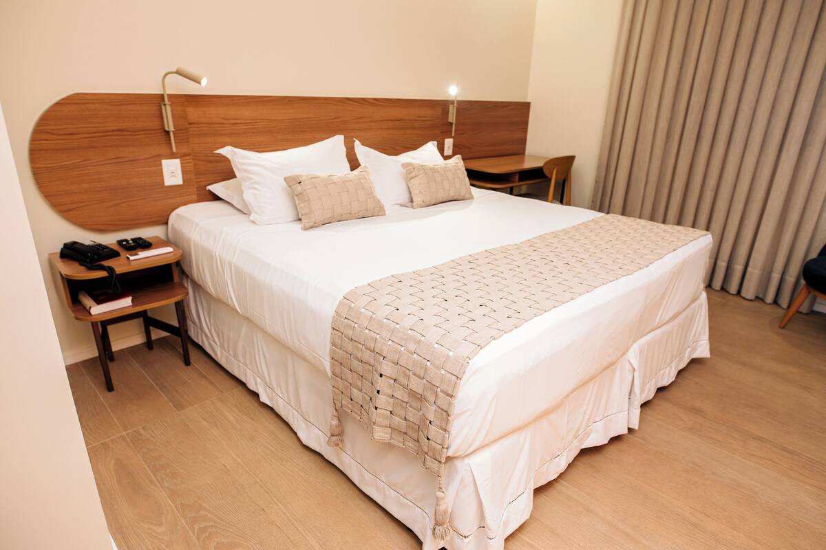 Uma cama bem arrumada com cabeceira de madeira, uma mesa de cabeceira com abajur e uma cadeira.
