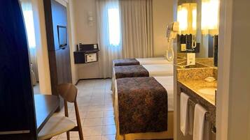 Quarto de hotel com cama, mesa de cabeceira, cadeira e pequena escrivaninha com luminária.