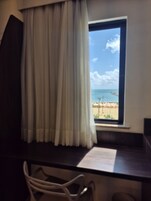 Quarto com escrivaninha, cadeira e janela com vista para a praia.