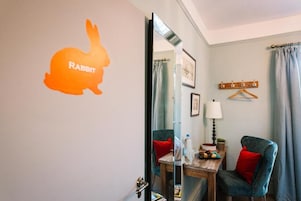 Quarto de hotel com espelho refletindo um banheiro, mesa de madeira com abajur e duas cadeiras.