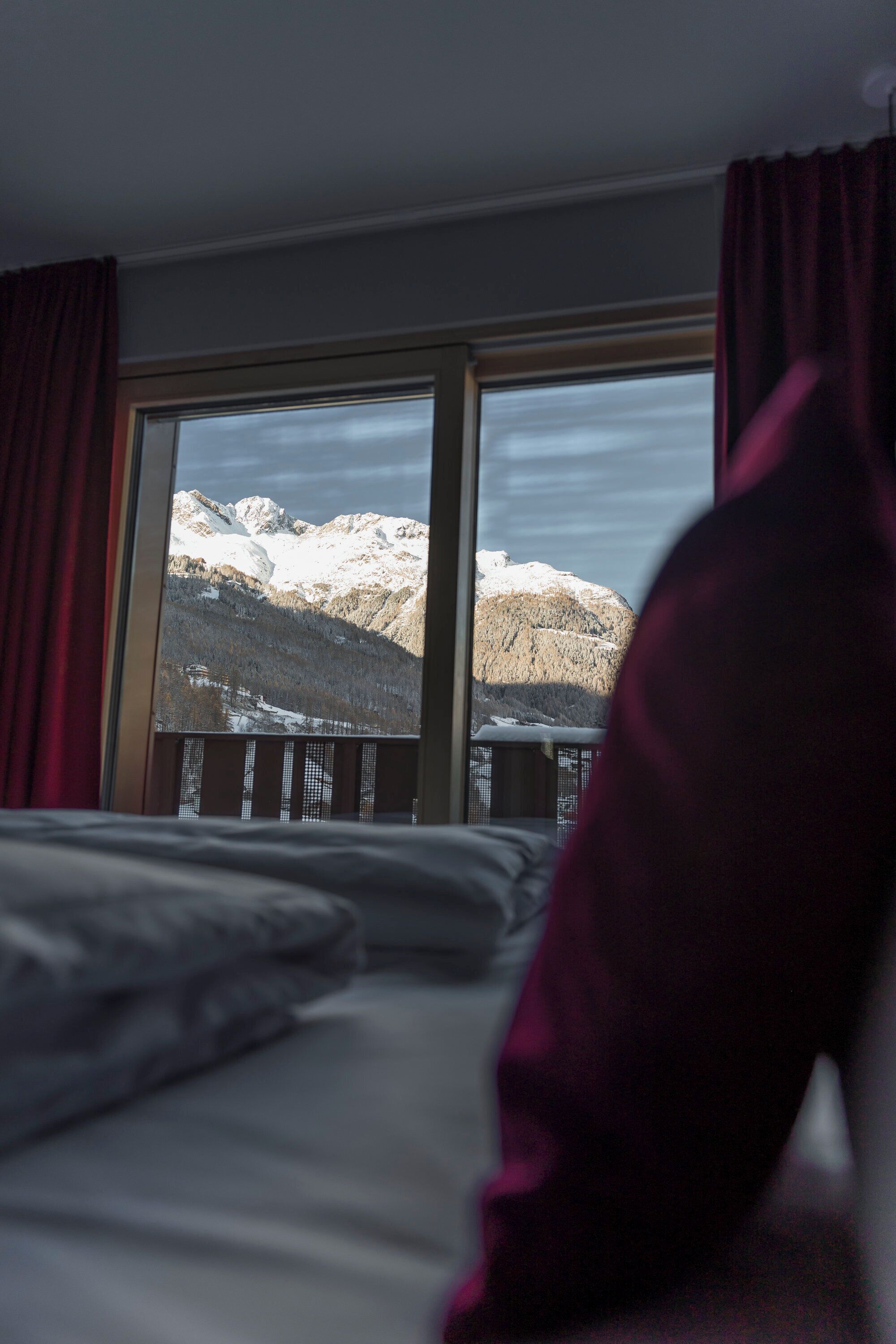 Quarto de hotel com uma grande janela que oferece vista para montanhas nevadas.