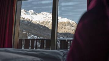 Quarto de hotel com uma grande janela que oferece vista para montanhas nevadas.