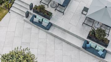Uma área de piscina no terraço com espreguiçadeiras e guarda-sóis, um pequeno espaço de estar com almofadas e um cercado de madeira delimitando o espaço.