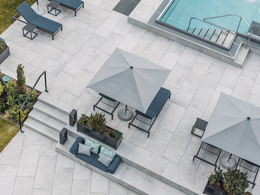 Uma área de piscina no terraço com espreguiçadeiras e guarda-sóis, um pequeno espaço de estar com almofadas e um cercado de madeira delimitando o espaço.