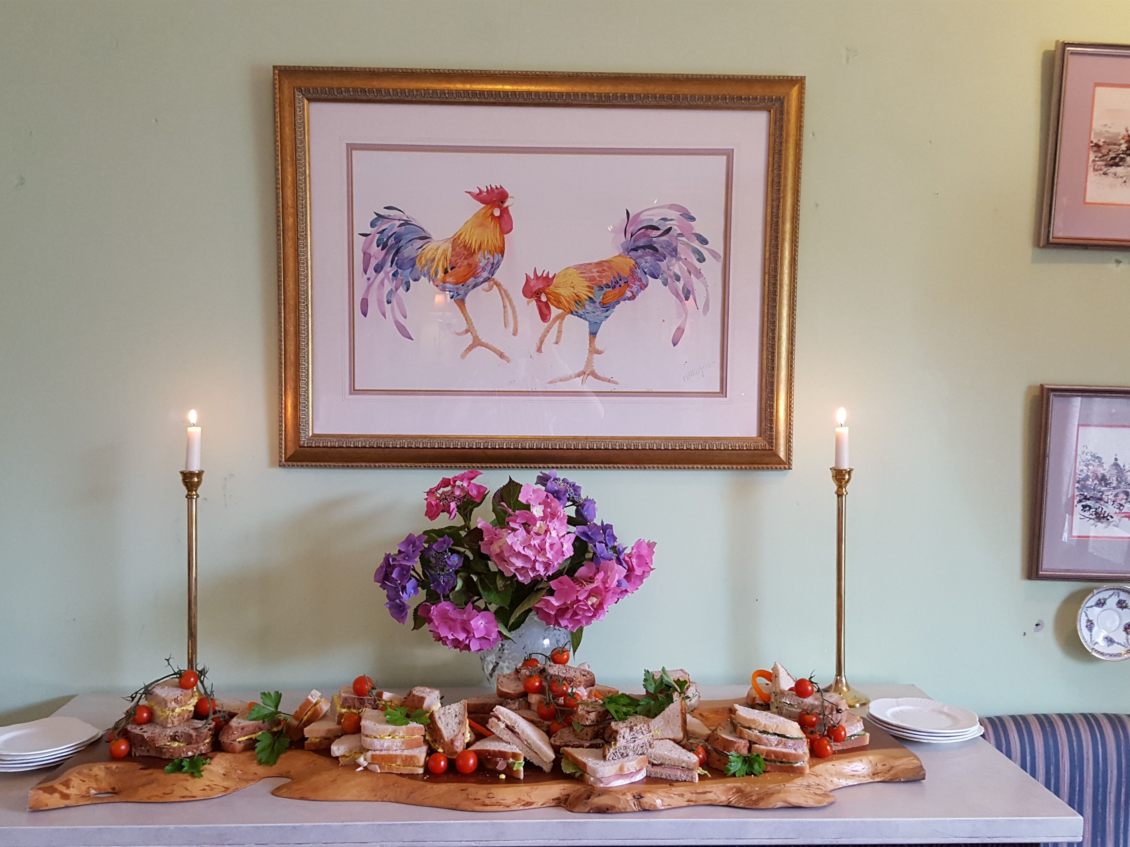 Uma mesa com sanduíches e tomates cereja, um vaso de flores e duas velas acesas.