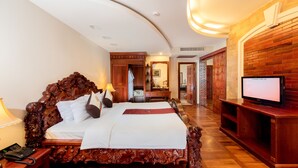 Um quarto espaçoso com uma cama grande, cabeceira de madeira, uma TV sobre suporte de madeira e telefone ao lado da cama.