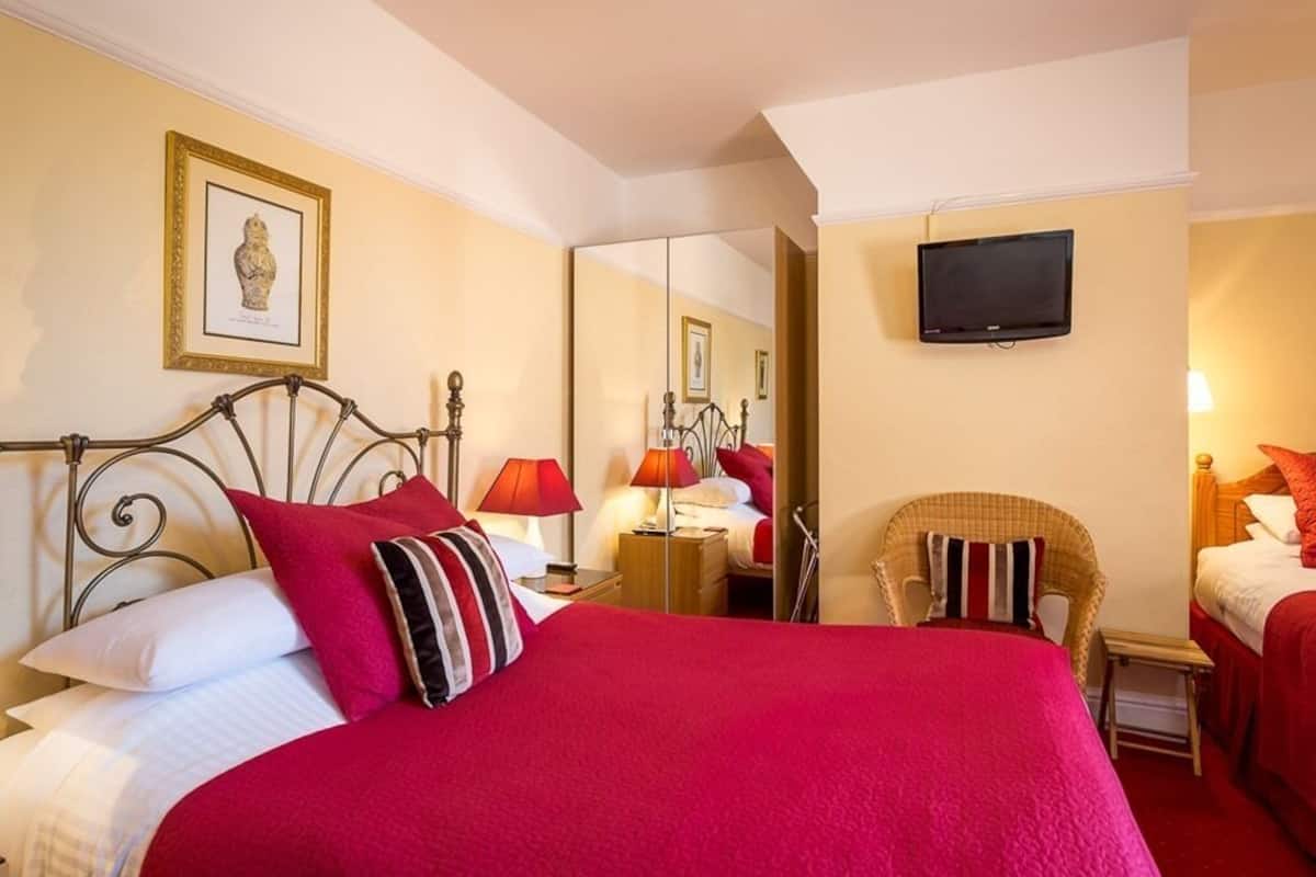 Quarto de hotel com uma cama grande, televisão fixada na parede, uma cadeira e uma mesa de cabeceira com luminárias.