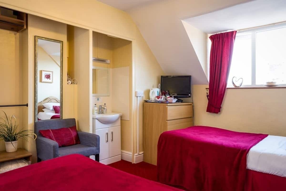 Quarto de hotel com duas camas, televisão, escrivaninha, espelho, pia e janela com cortinas.