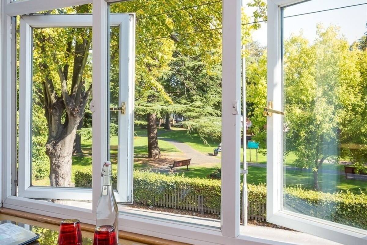 Quarto com uma grande janela com vista para um parque com árvores e um banco.