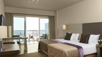 Quarto de hotel com uma cama grande, uma escrivaninha, uma cadeira e uma varanda com vista.
