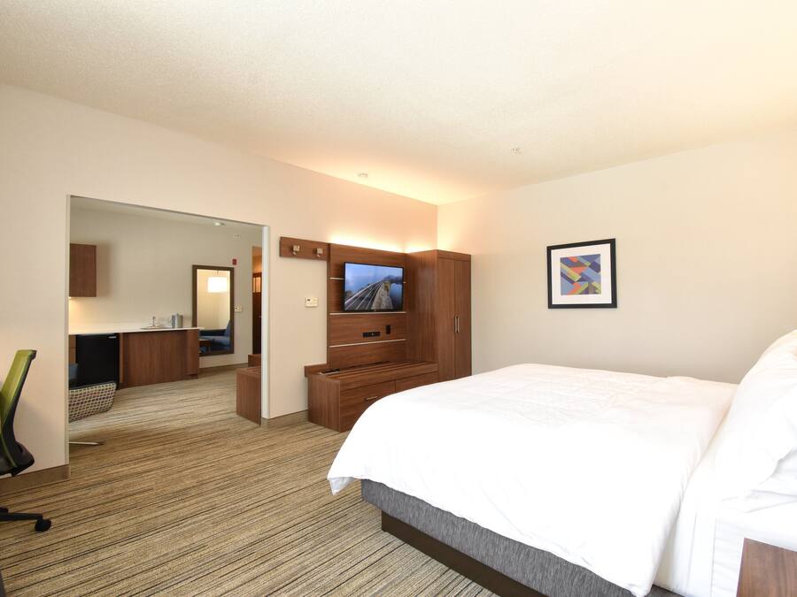 Quarto de hotel com uma cama grande, uma escrivaninha, uma cadeira, uma televisão e um quadro na parede.
