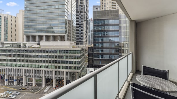 Varanda com mesa e cadeiras, vista para um horizonte urbano com edifícios modernos e um estacionamento.