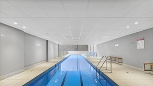 Uma grande piscina interior com pistas demarcadas, piso revestido e um aviso com as 'REGRAS DA PISCINA' na parede.