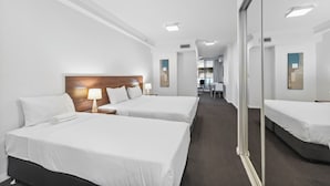 Quarto de hotel com duas camas, cabeceira de madeira, um espelho e uma escrivaninha com cadeira.