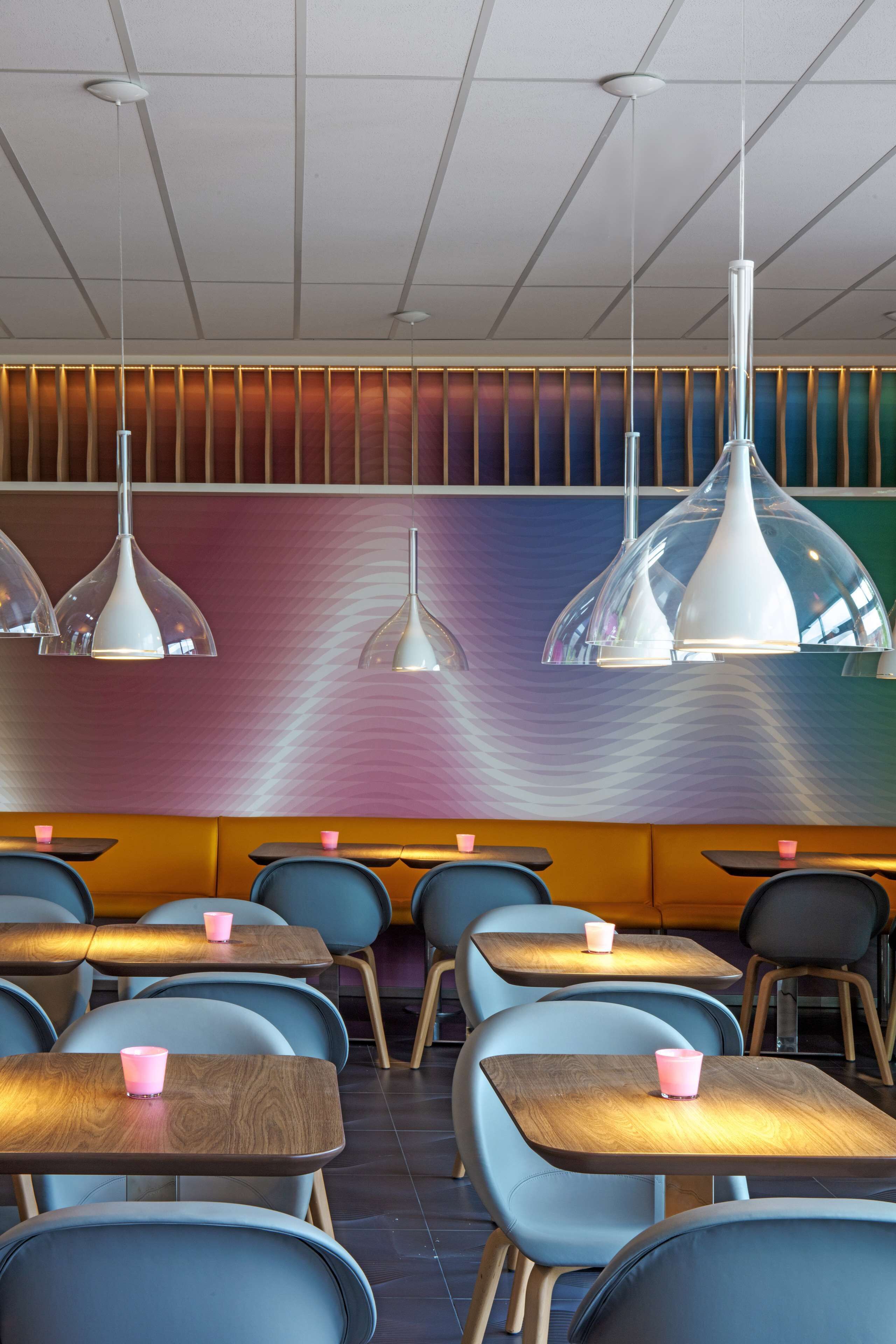 Interior de restaurante com cabines e mesas, iluminação pendente e um design de parede colorido.