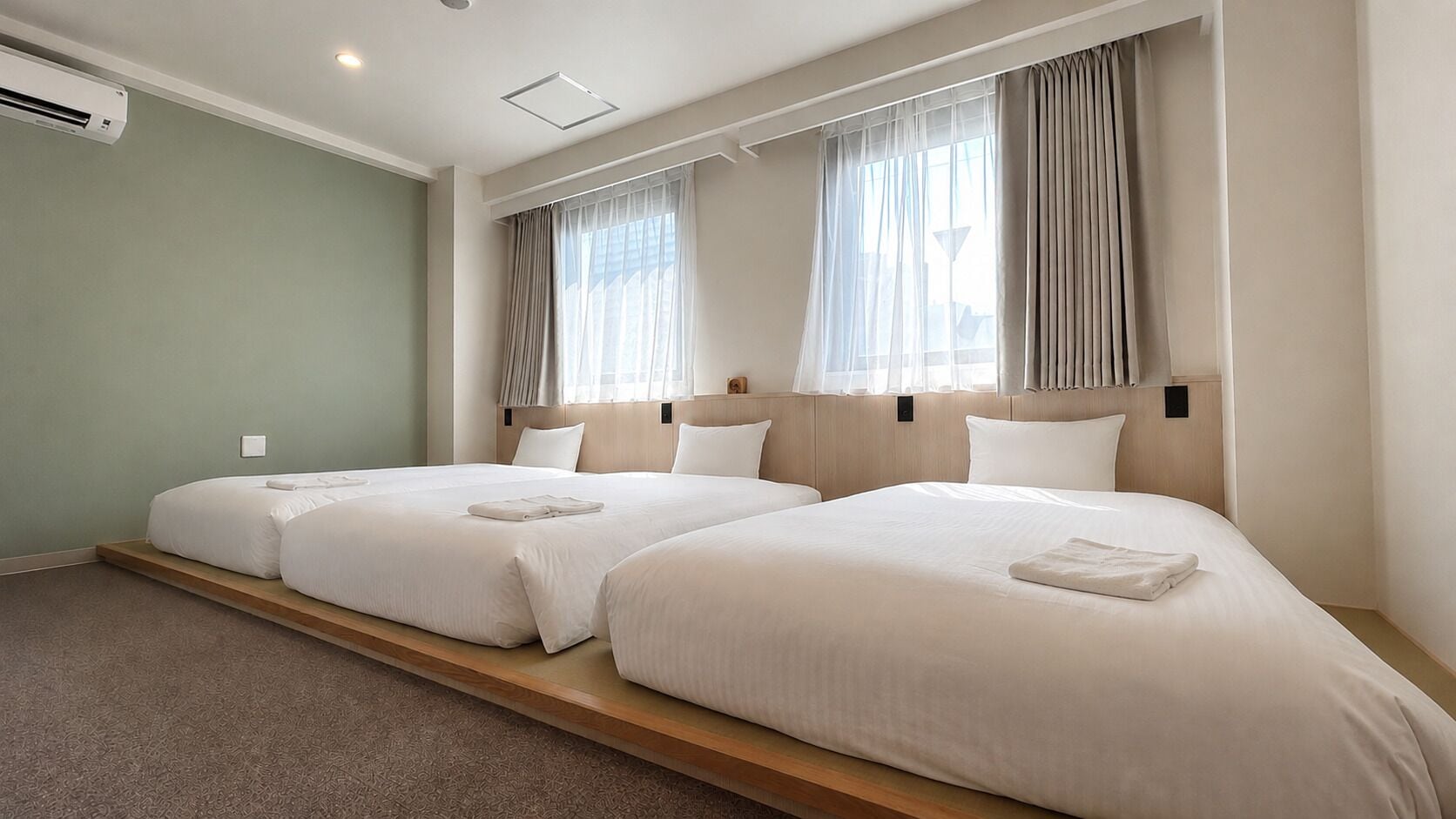 Quarto de hotel com duas camas, uma plataforma de madeira e uma janela com cortinas.