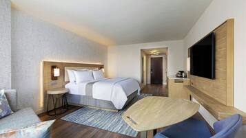 Quarto de hotel com cama, televisão, mesa pequena, cadeira e escrivaninha.