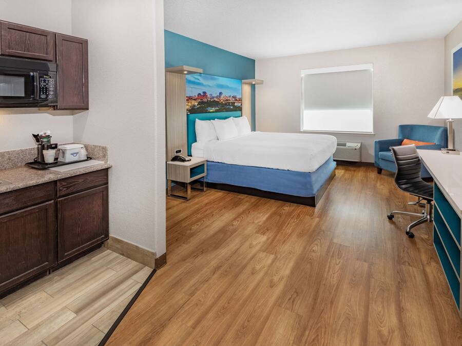 Quarto de hotel com cama, escrivaninha, cadeira, micro-ondas, torradeira e pia.