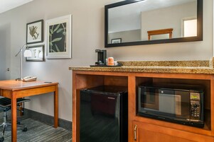 Quarto de hotel com escrivaninha, cafeteira, geladeira e micro-ondas.