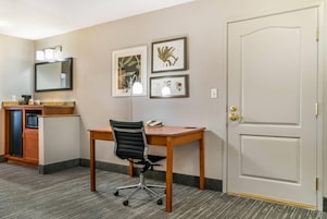 Quarto de hotel com escrivaninha, cadeira, cozinha compacta e porta.