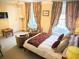 Quarto com cama, cadeira, mesa, abajur e cortinas.