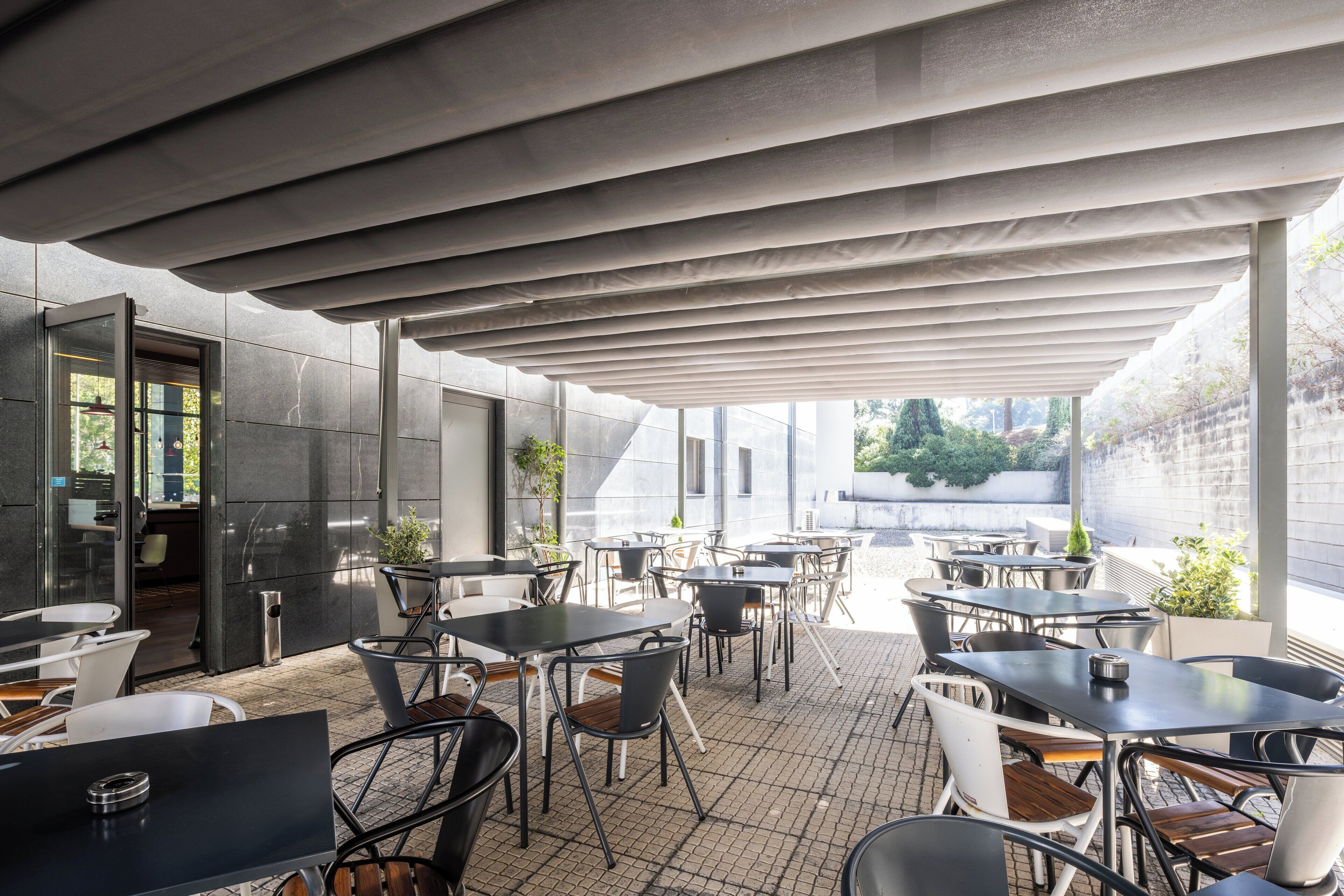 Um café ao ar livre com mesas e cadeiras, área de estar coberta e vista para a rua.