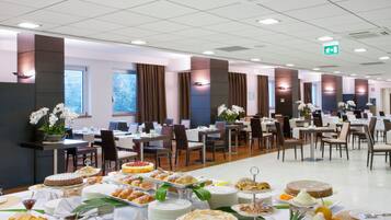 Espaço de refeições de hotel com várias mesas, cadeiras, sobremesas e doces.