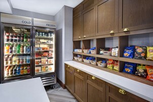 Uma área de cozinha com geladeira identificada como 'COLD' e 'FROZEN', repleta de bebidas e petiscos.