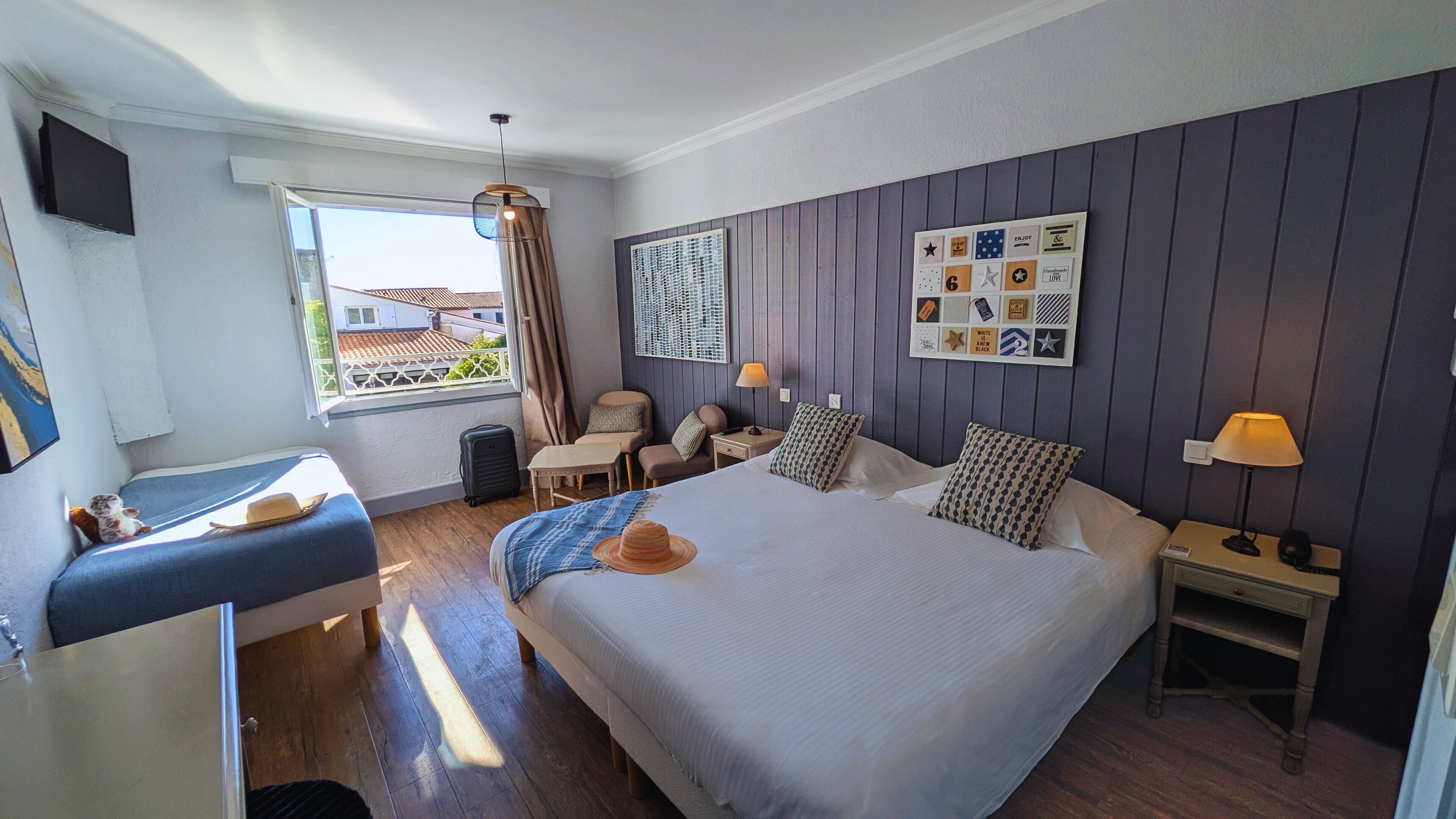 Quarto de hotel com uma cama grande, uma escrivaninha, uma cadeira, uma televisão e uma janela com vista para edifícios.